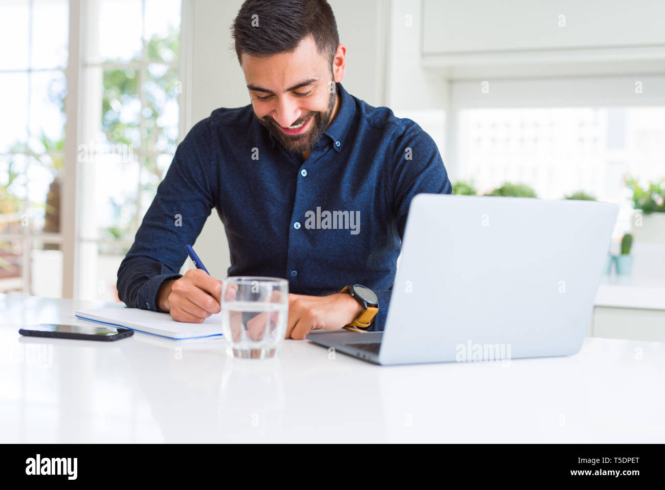 Handsome hispanic man working using computer and writing on a paper ...