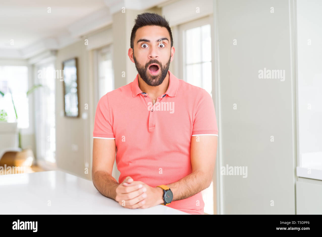 Handsome hispanic man wearing casual t-shirt at home afraid and shocked ...