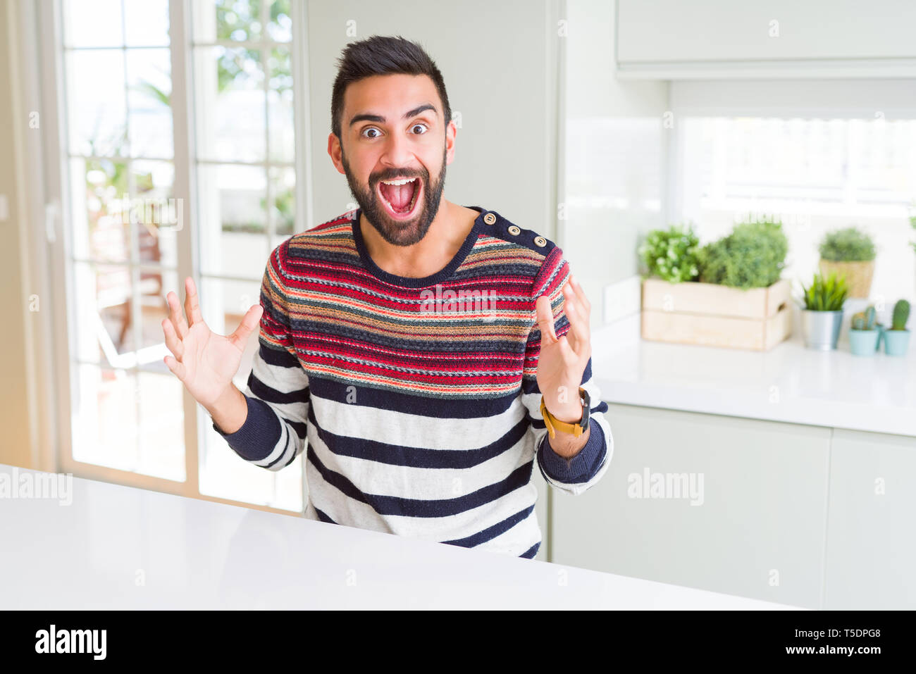 Handsome hispanic man wearing stripes sweater at home celebrating crazy ...