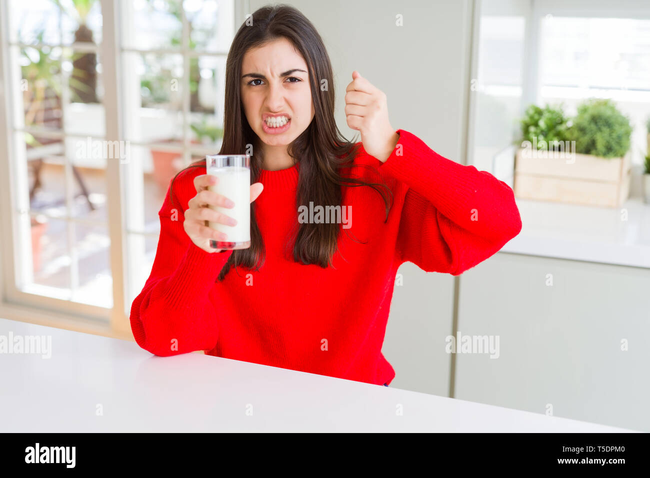 Beautiful young woman drinking a glass of fresh milk annoyed and ...