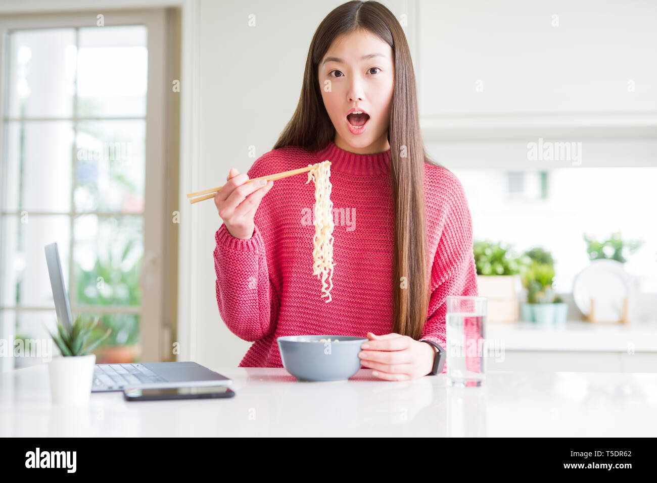 Beautiful Asian woman working using laptop and eating asian noodles ...