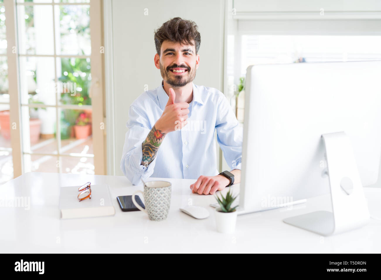 Young business man working using computer doing happy thumbs up gesture ...