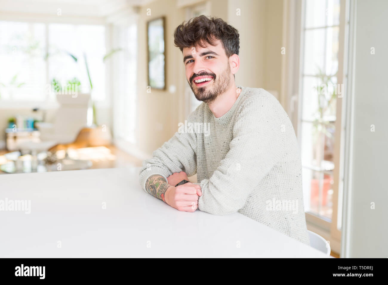 Handsome young man smiling cheerful at the camera with crossed arms and ...