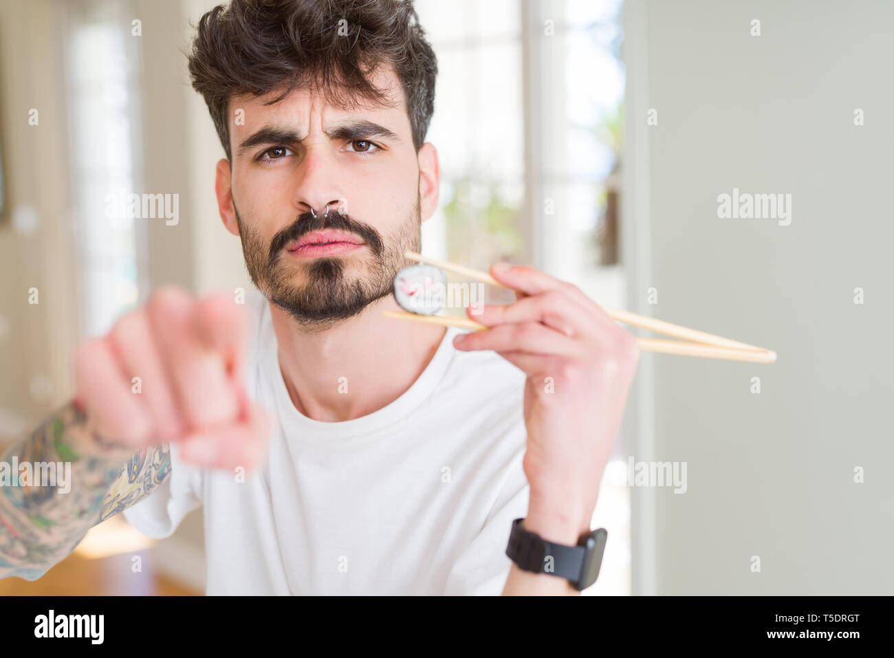 Young man eating asian sushi using chopsticks pointing with finger to ...