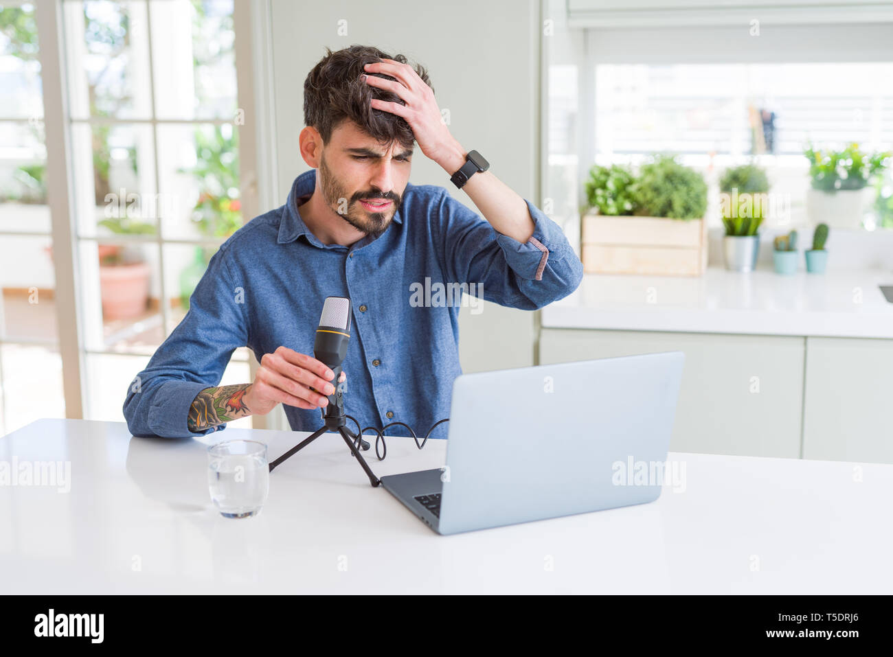 Young man recording podcast using microphone and laptop stressed with ...