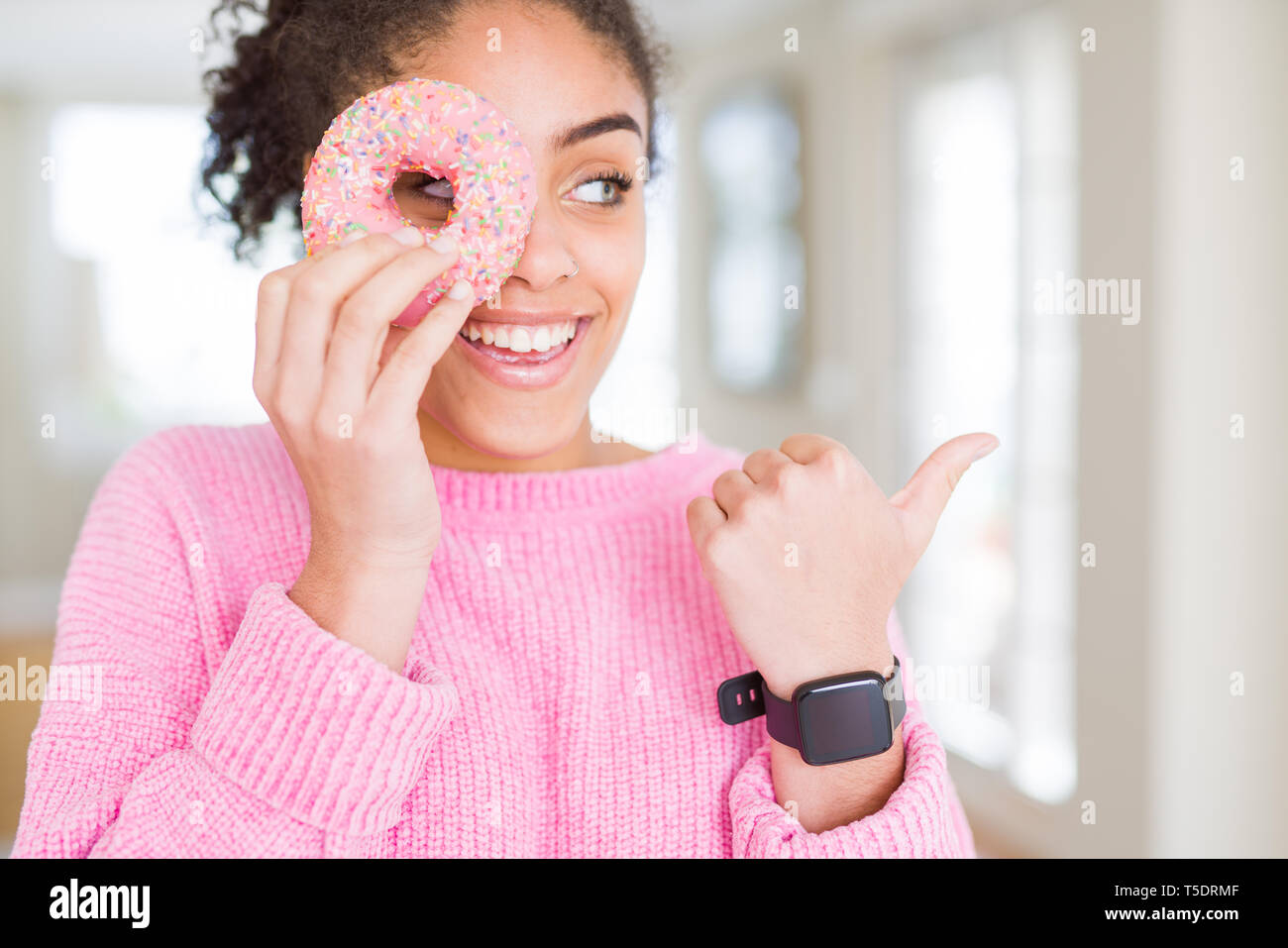 Young african american girl eating sweet pink donut pointing and ...