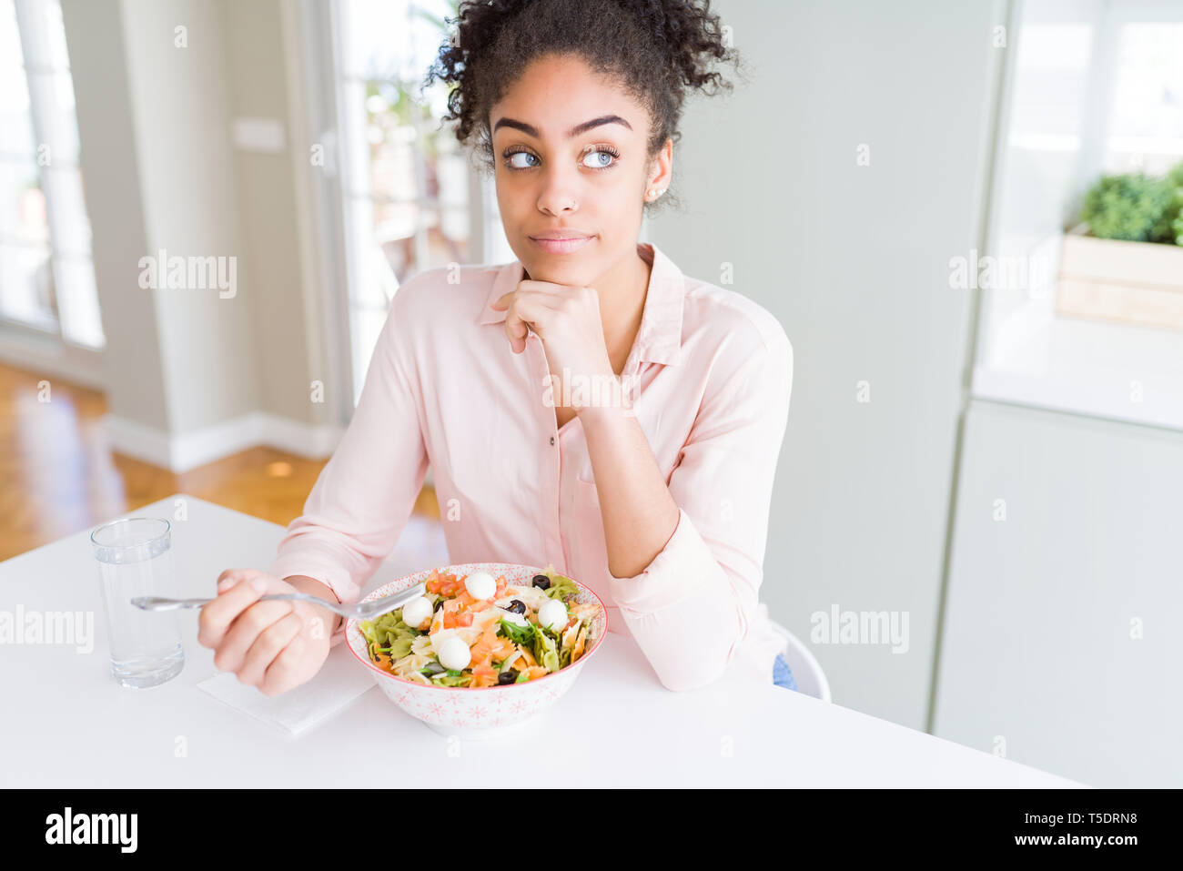Young african american woman eating healthy pasta salad serious face ...
