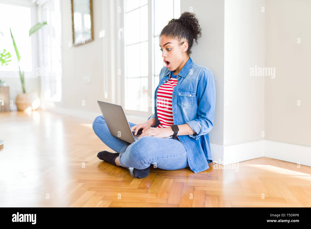 Young african american woman sitting on the floor using computer laptop ...