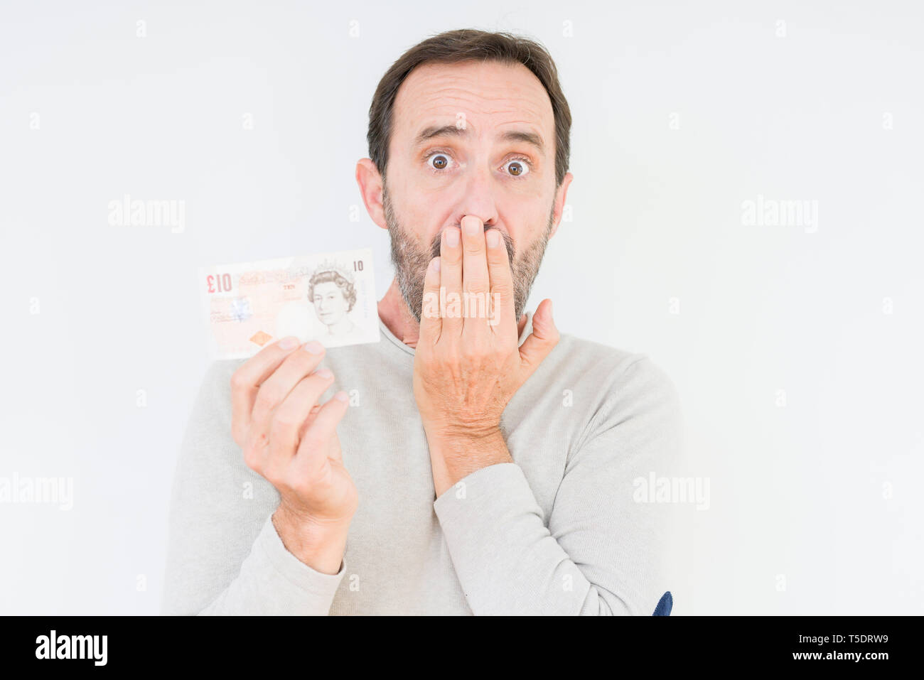 Senior man holding ten pounds bank note over isolated background cover ...