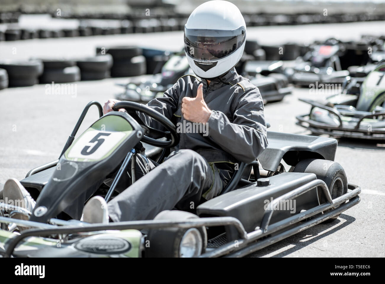 Racer in sportswear and protective helmet driving go-kart on the track ...