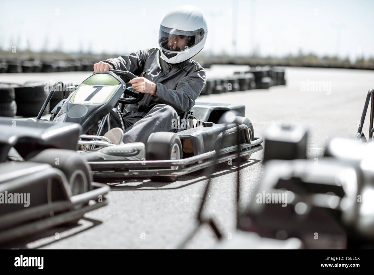 Racer in sportswear and protective helmet driving go-kart on the track ...