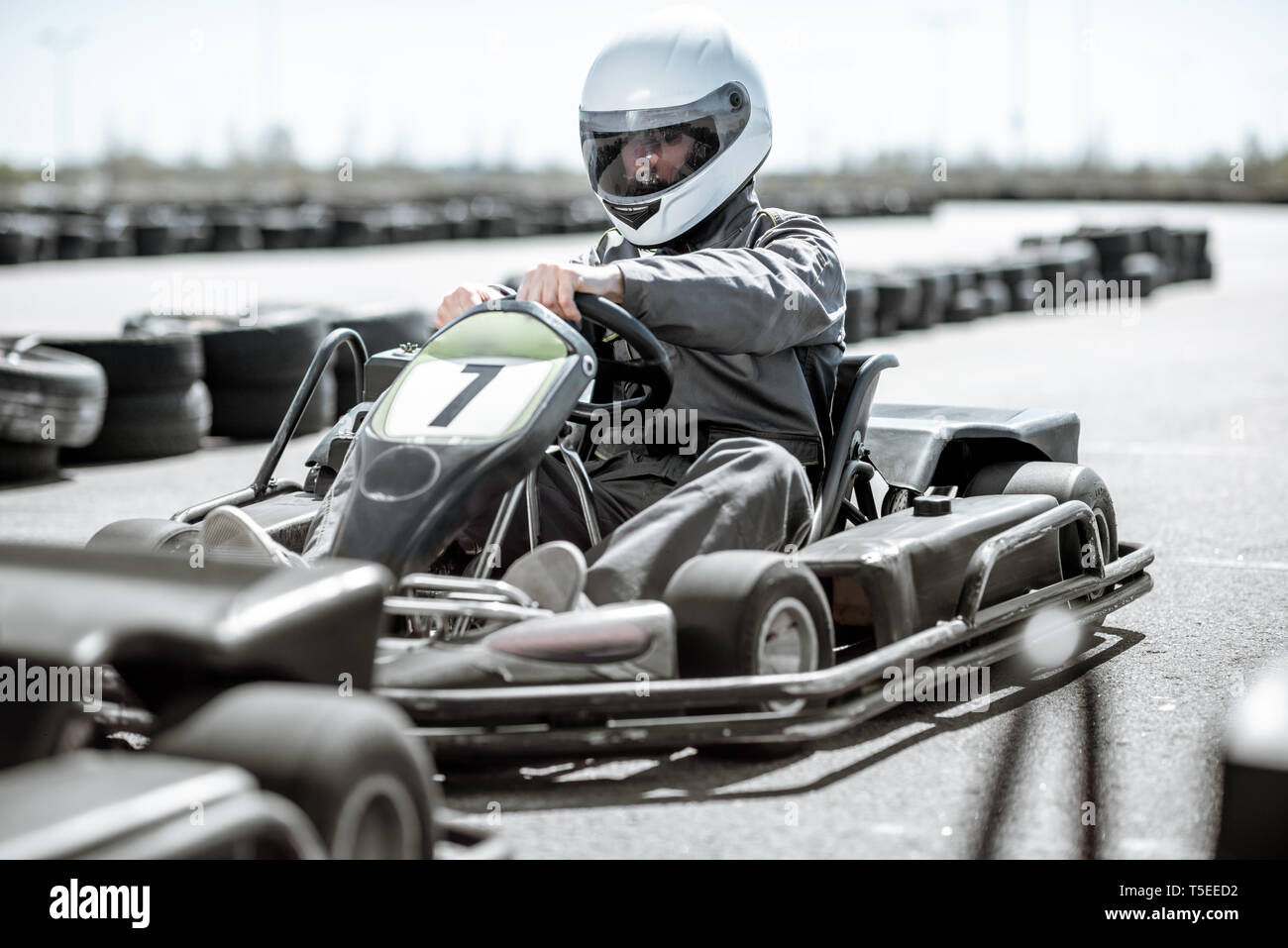 Racer in sportswear and protective helmet driving go-kart on the track ...