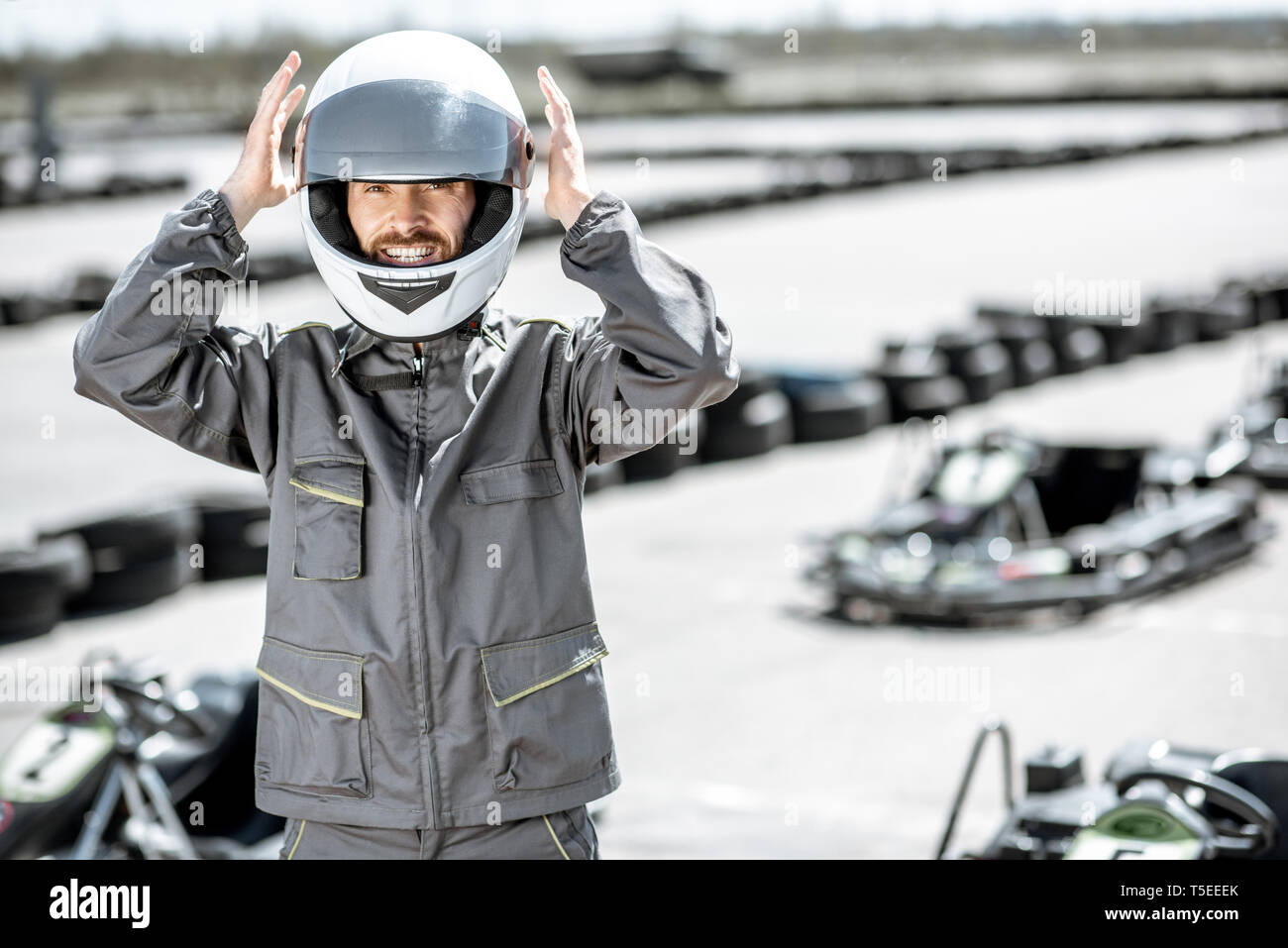 Portrait of a happy male racer in uniform wearing protective helmet ...
