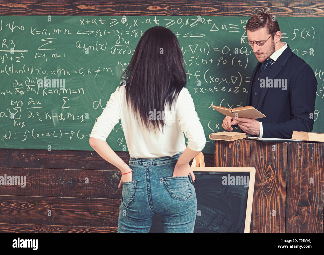 Strict professor in glasses reading a book at rostrum. Female brunette ...