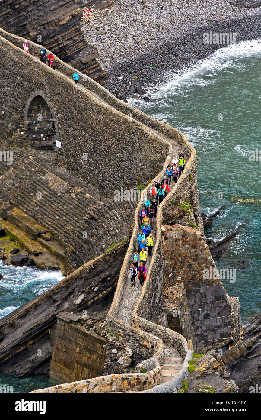 Visitors crossing teh stone bridge to the islet Gaztelugatxe near Bakio ...
