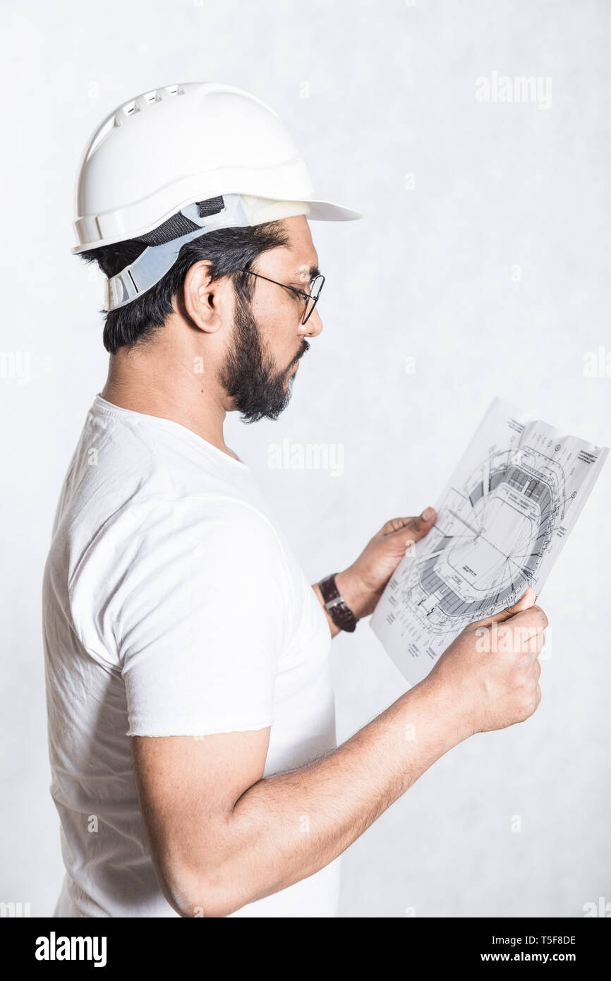 A young construction worker with glasses and a white protective helmet ...