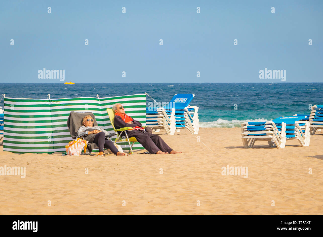 elderly couple asleep on deck chairs in front of wind break on beach at ...