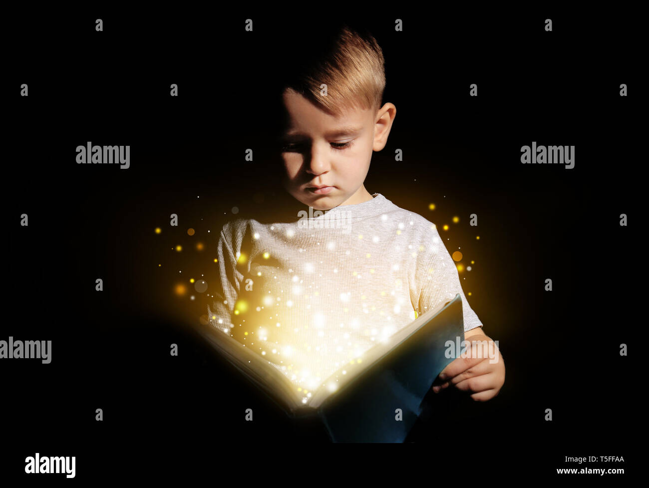 Cute little boy reading magic book on dark background Stock Photo - Alamy