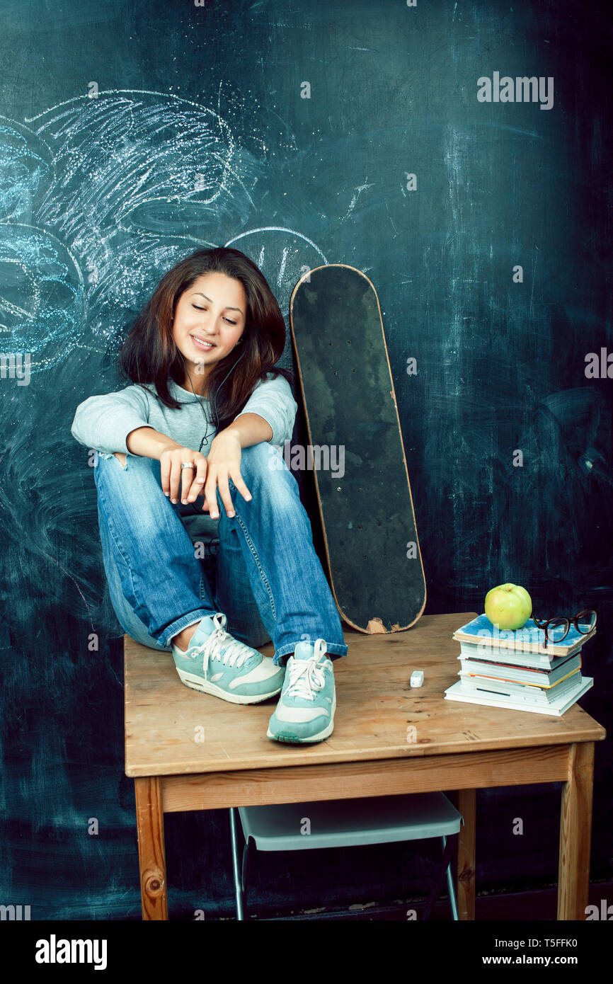 young cute teenage girl in classroom at blackboard seating on table ...