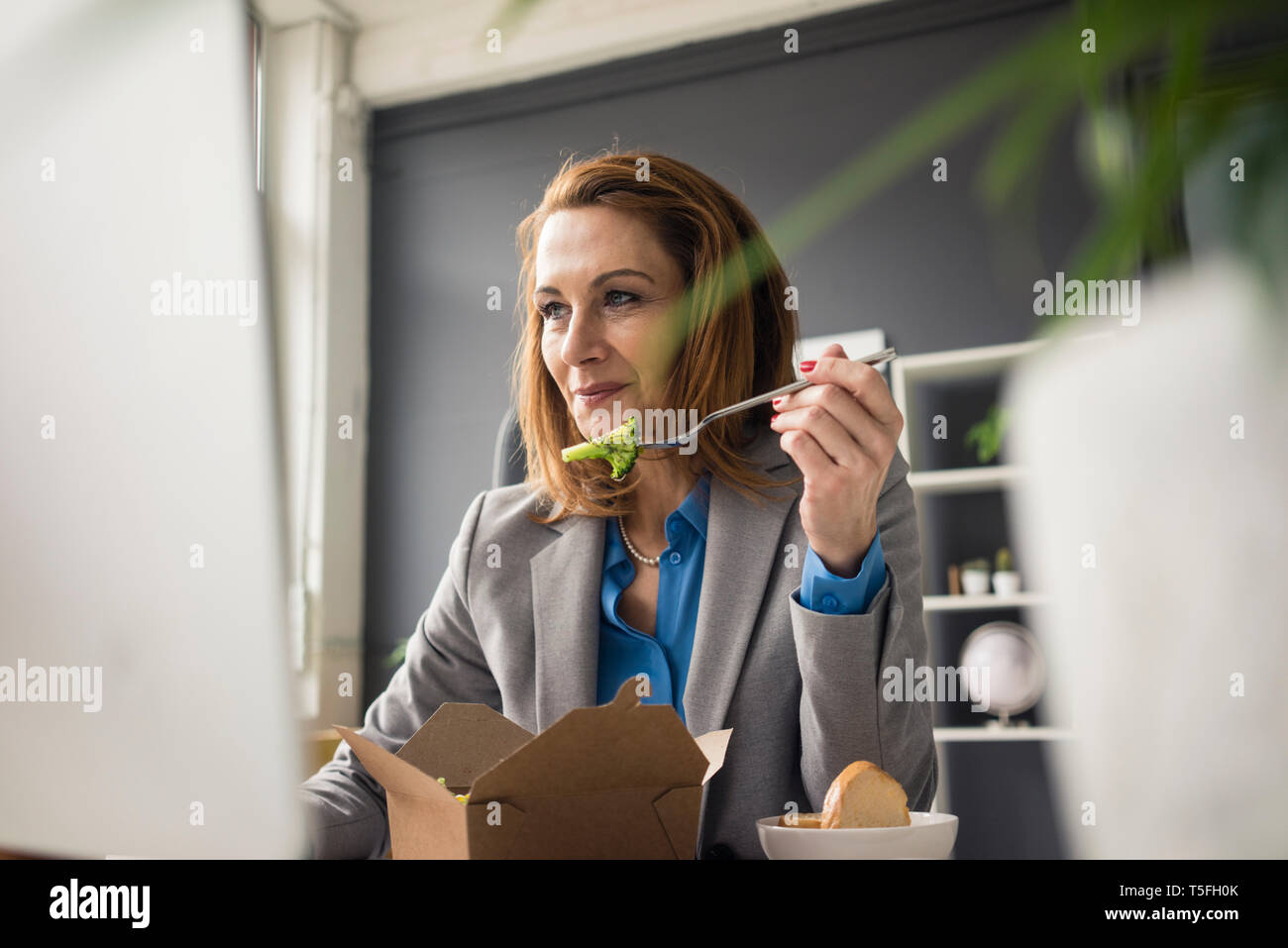 Businesswoman sitting in office, working on PC, eating lunch Stock ...