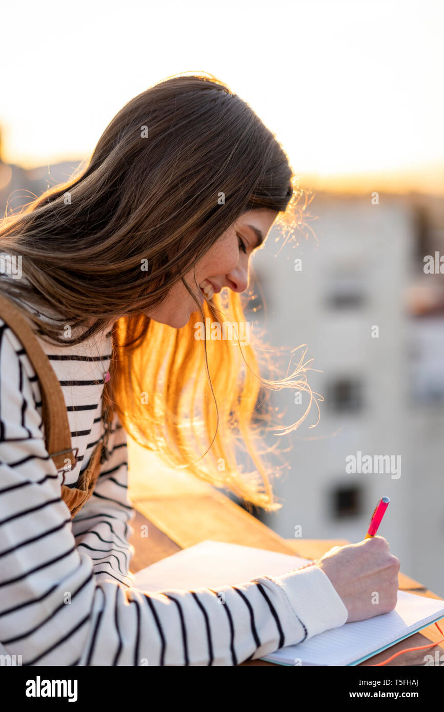 Happy young woman taking notes on roof terrace at sunset Stock Photo ...