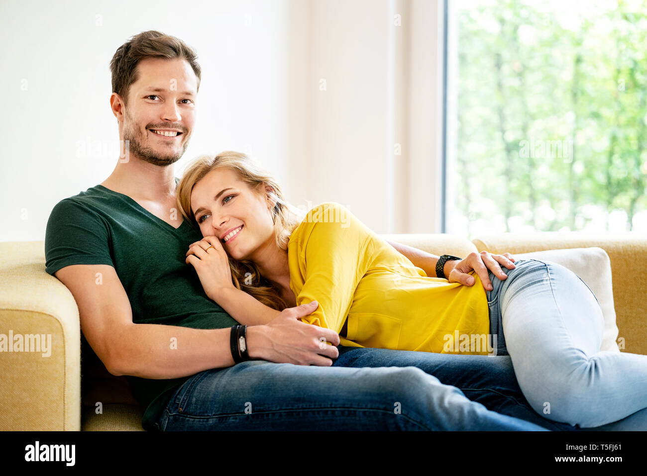 Couple sitting on couch in their new home, cuddling Stock Photo - Alamy