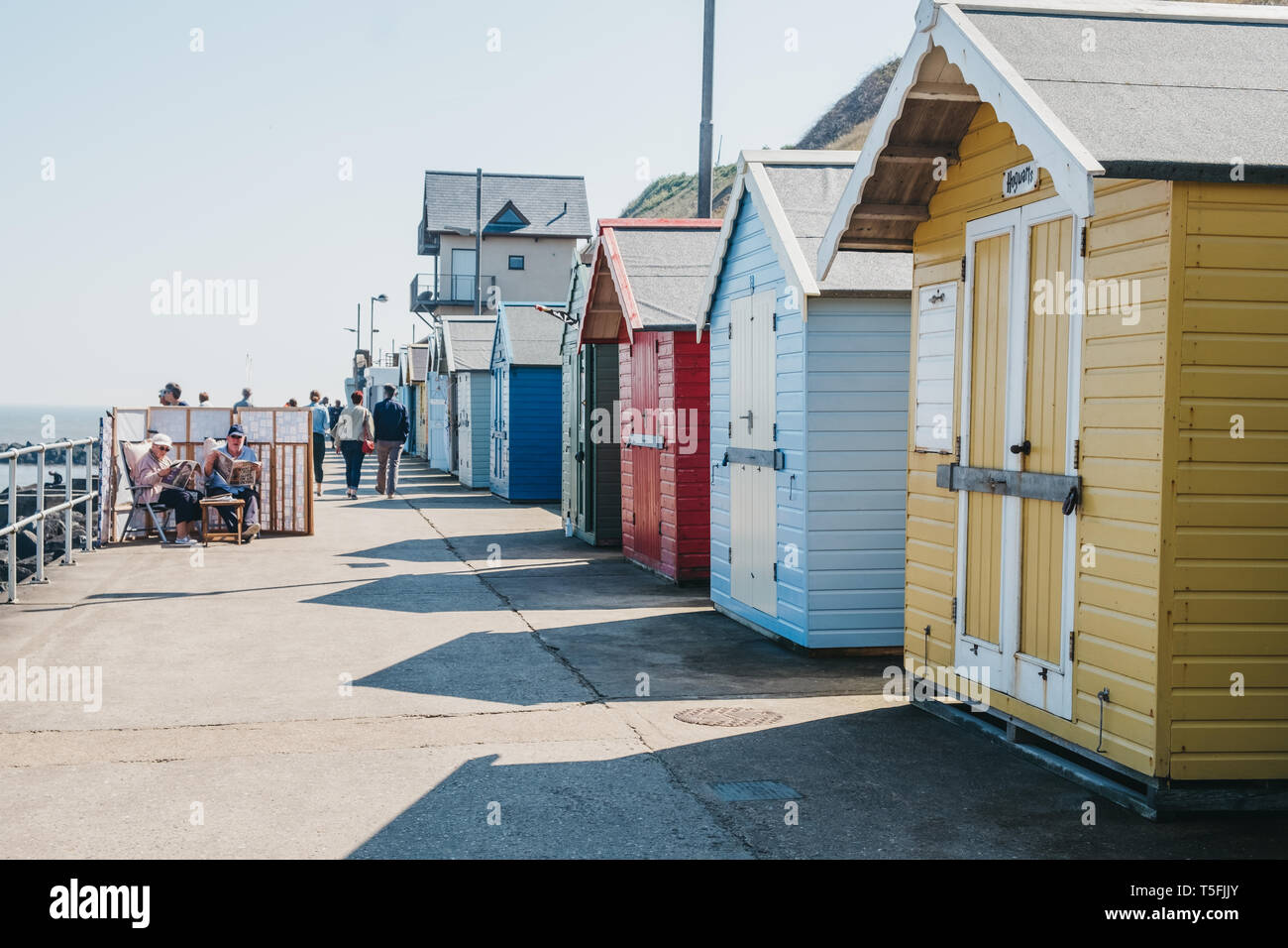 Sheringham, UK - April 21, 2019: People sitting by colourful beach huts ...