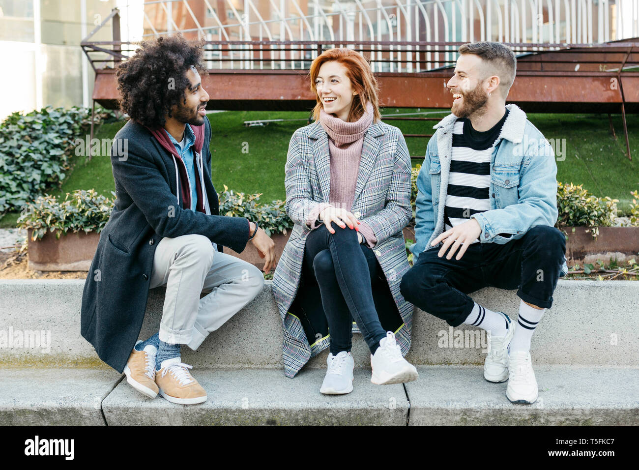 Three happy friends sitting in the city talking Stock Photo - Alamy