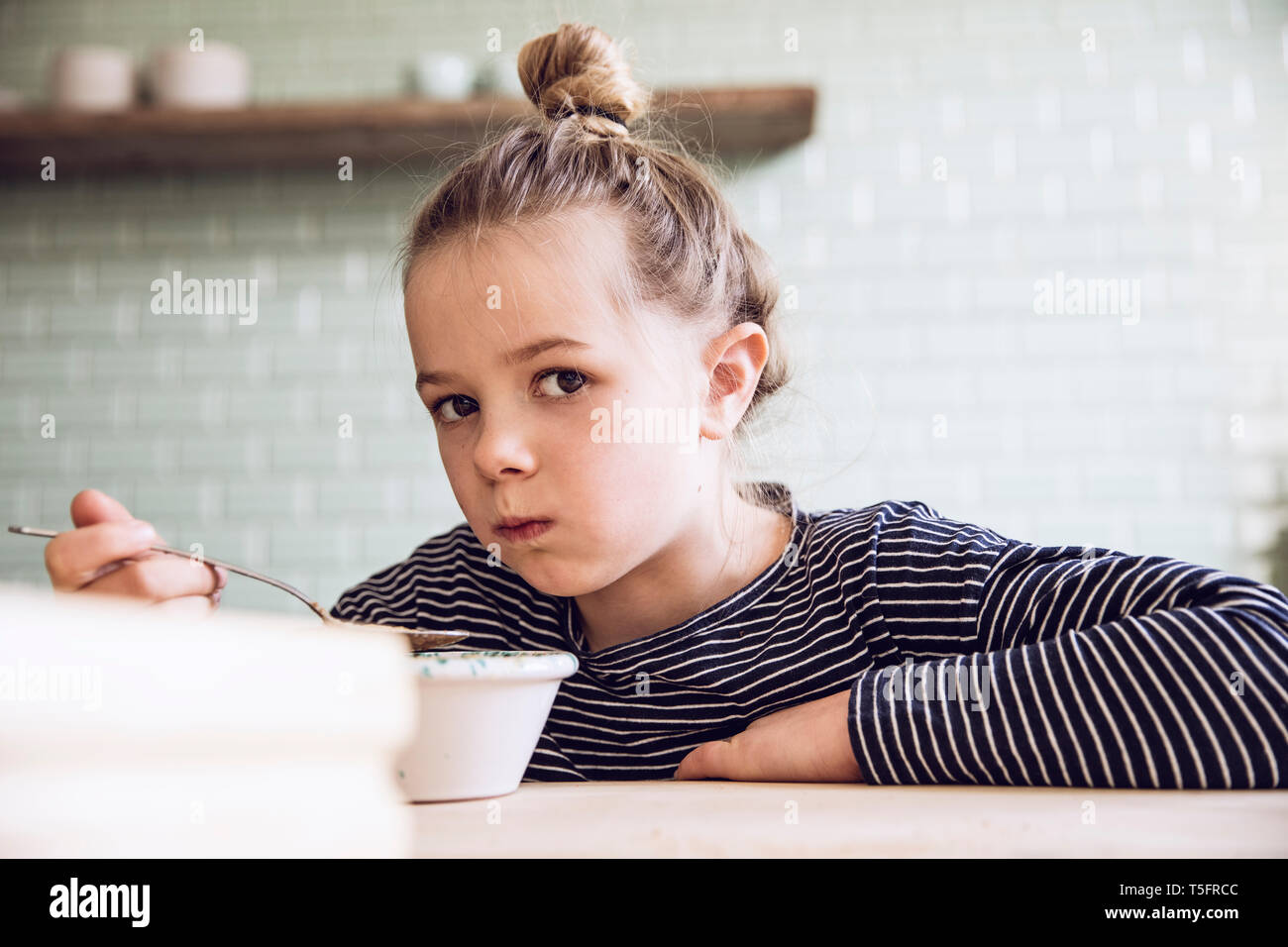 Sceptical girl sitting in kitchen, eating granola Stock Photo - Alamy