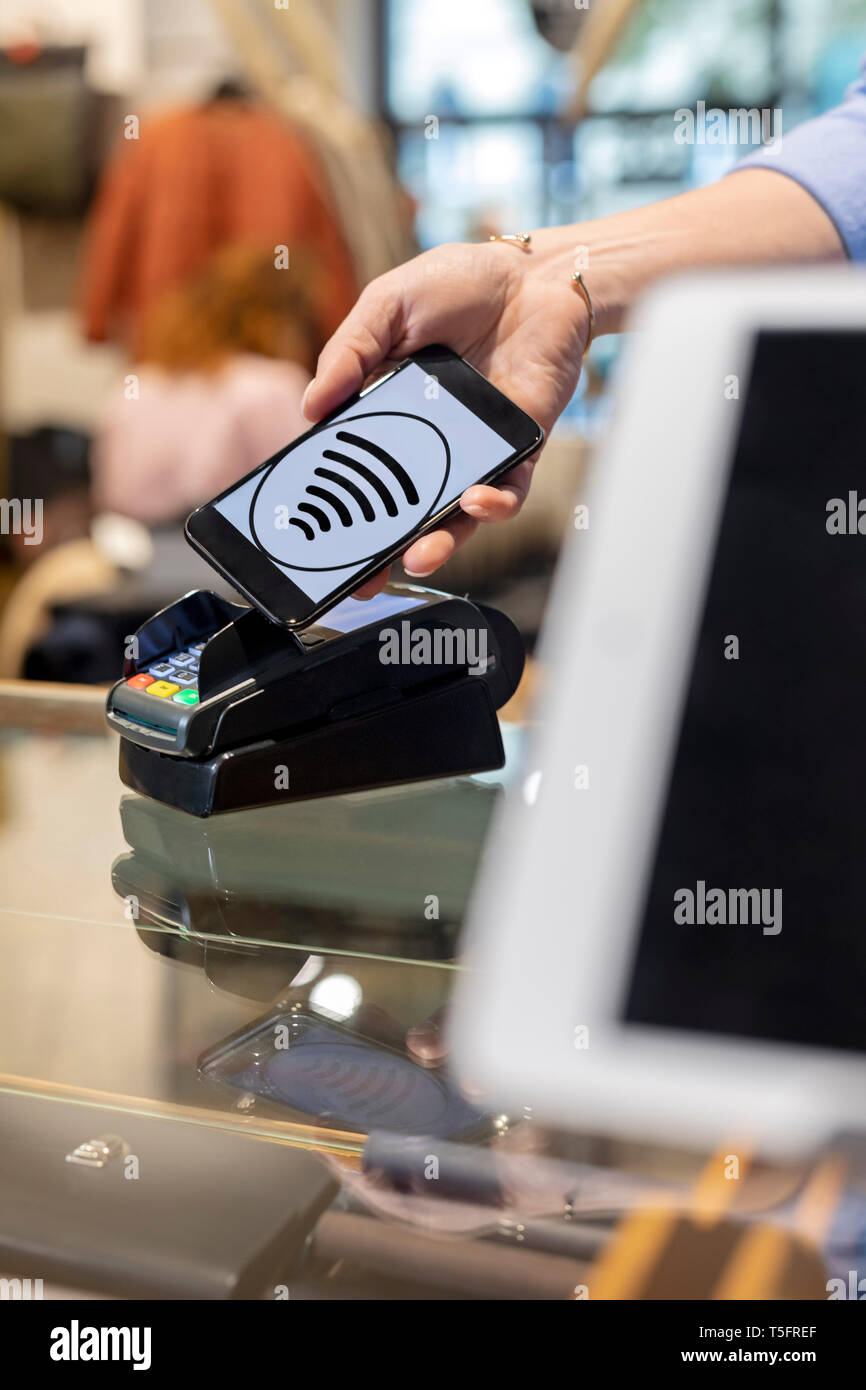 Customer paying contactless with smartphone in a fashion store Stock ...