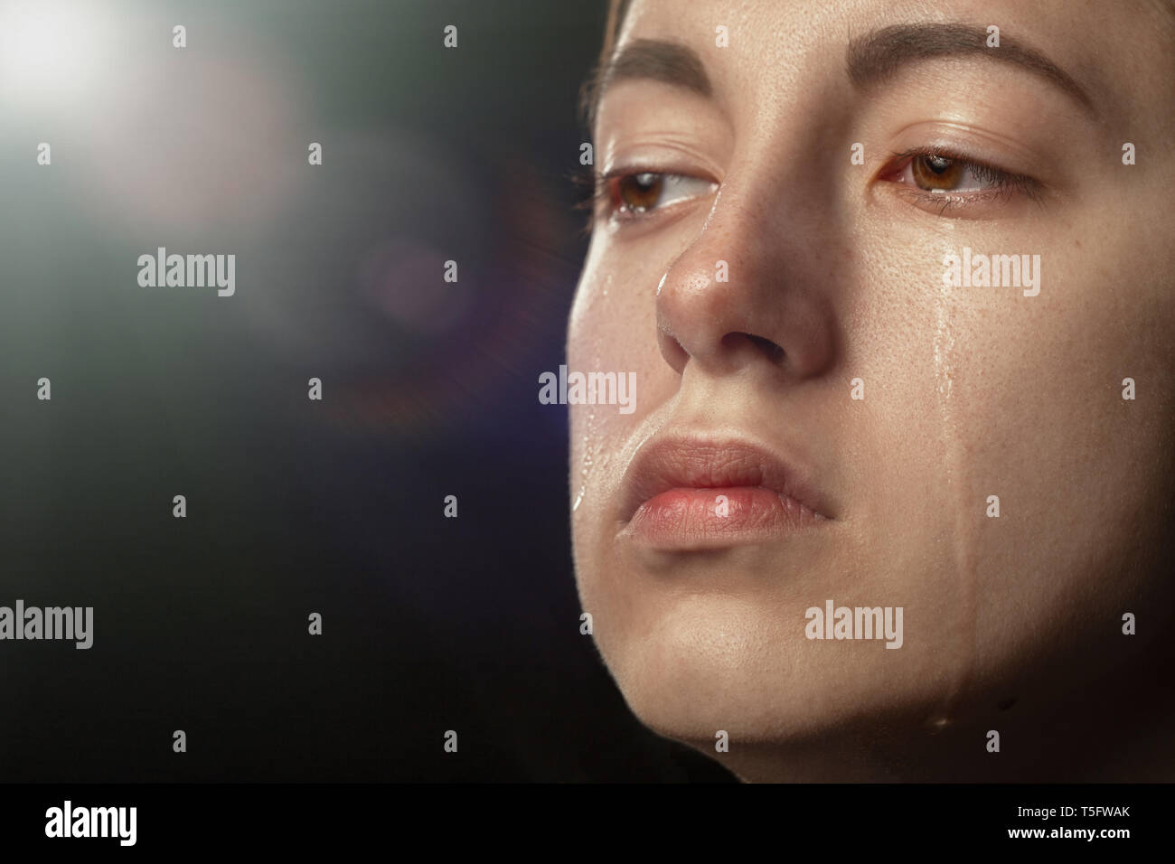 sad woman crying on black background with light rays, closeup portrait ...