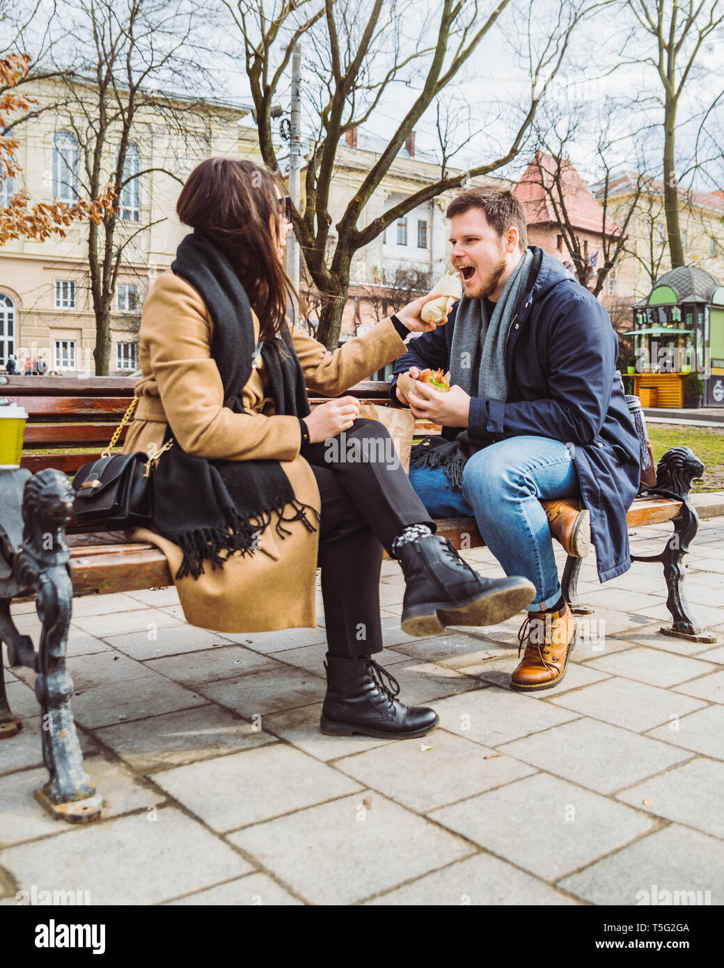 young adult couple eating fast food on bench of city park. lifestyle ...