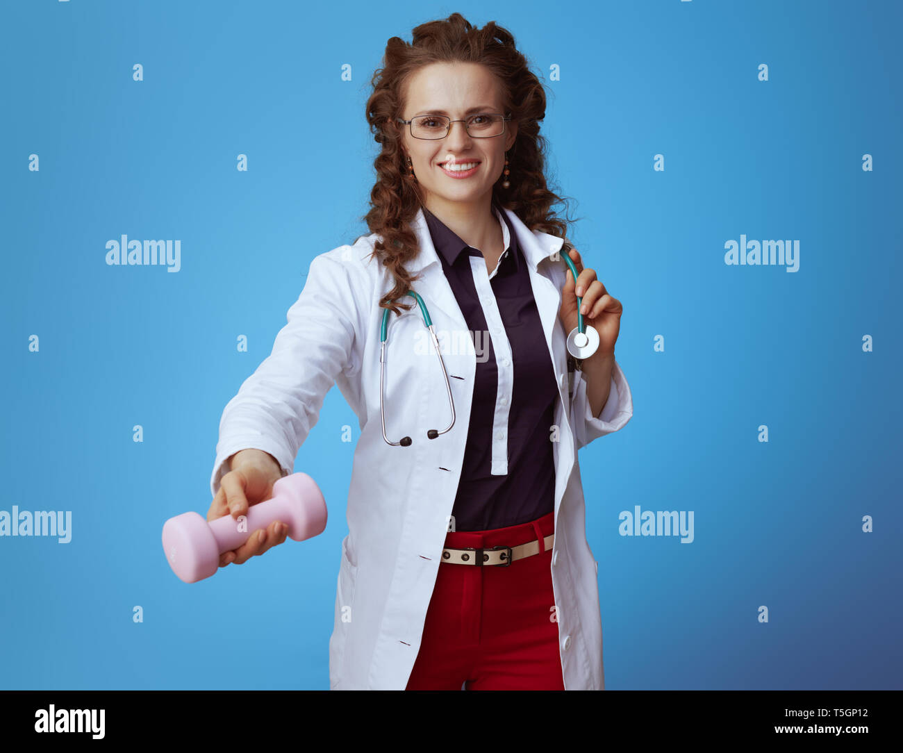 smiling elegant medical doctor woman in bue shirt, red pants and white ...