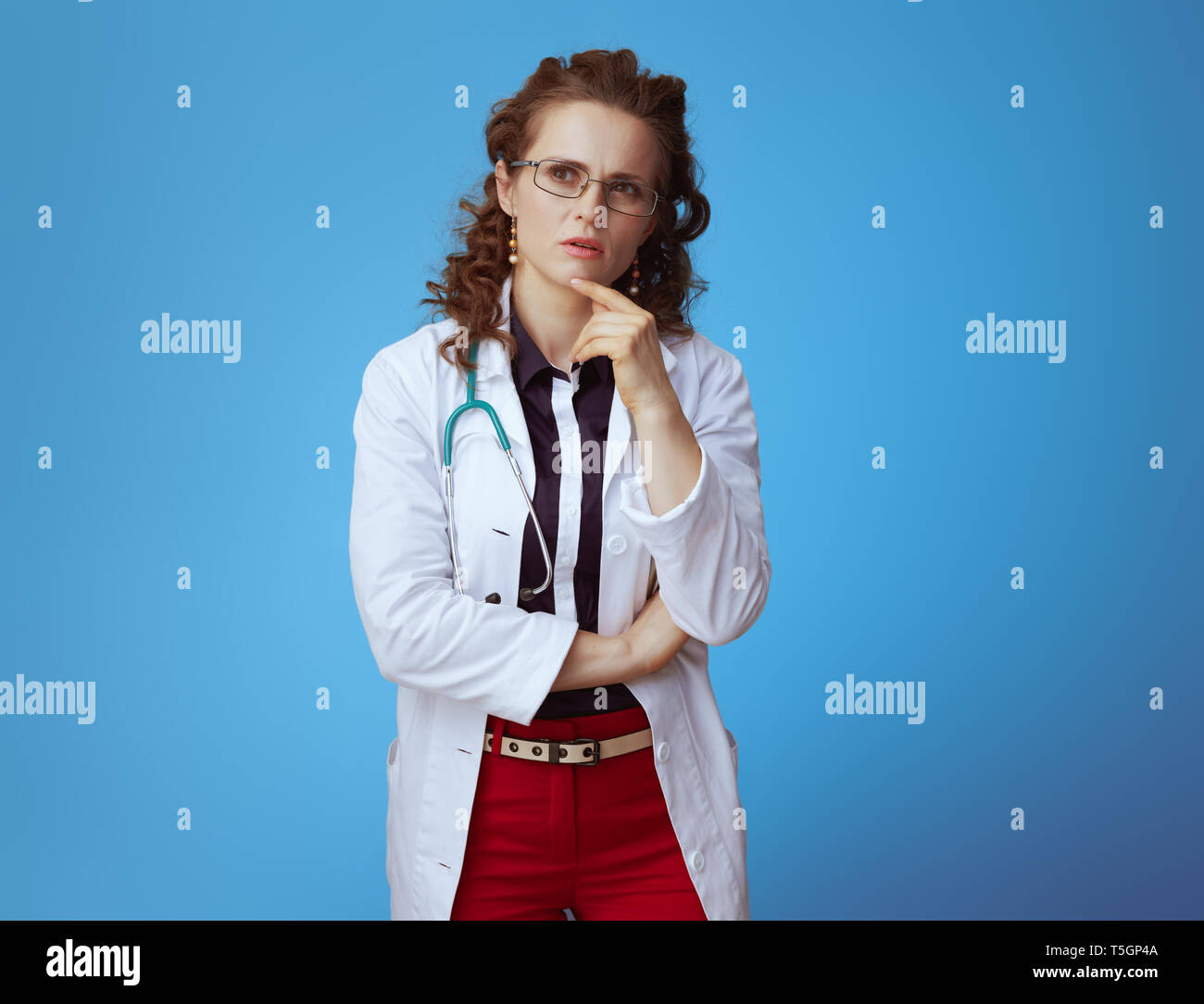 Portrait of pensive modern medical doctor woman in bue shirt, red pants ...