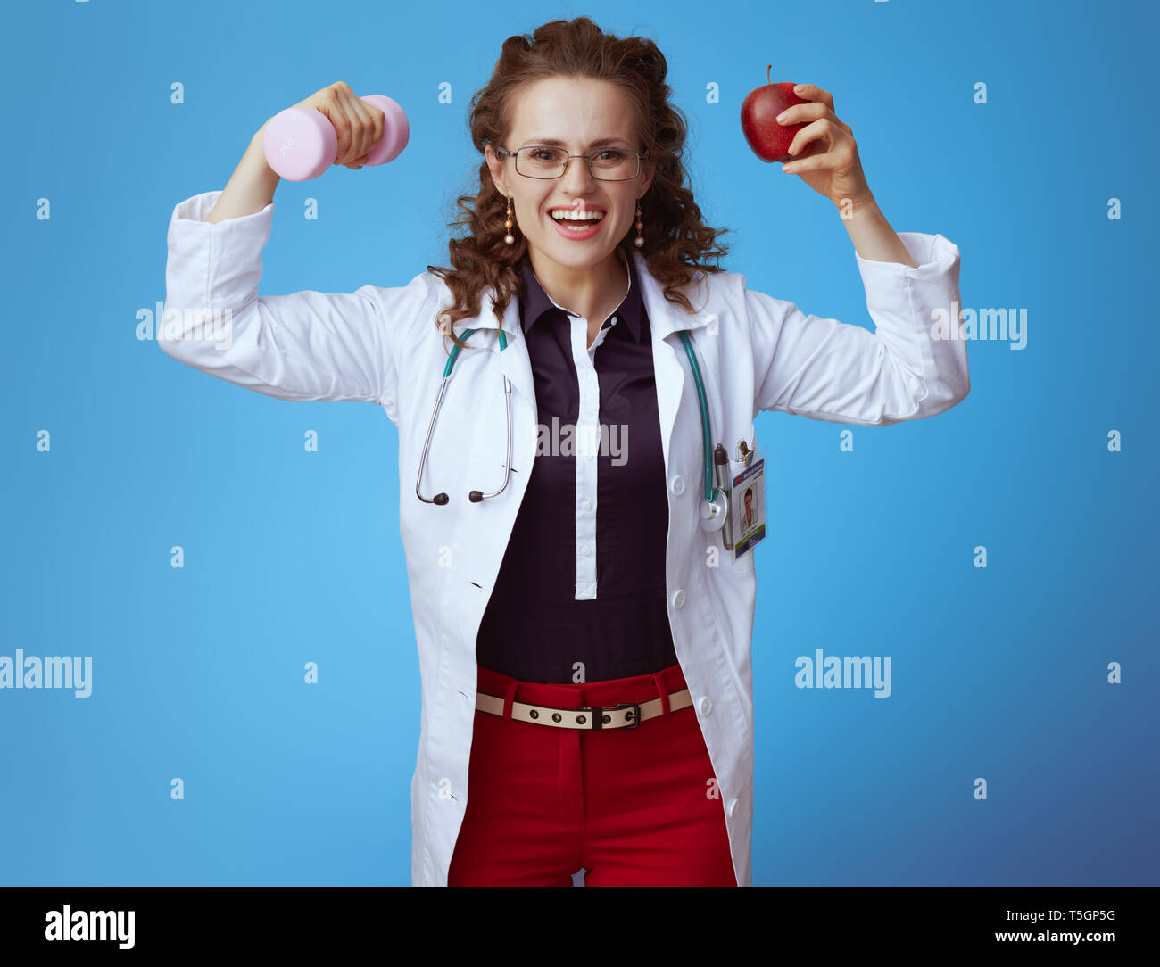 smiling elegant medical practitioner woman in bue shirt, red pants and ...
