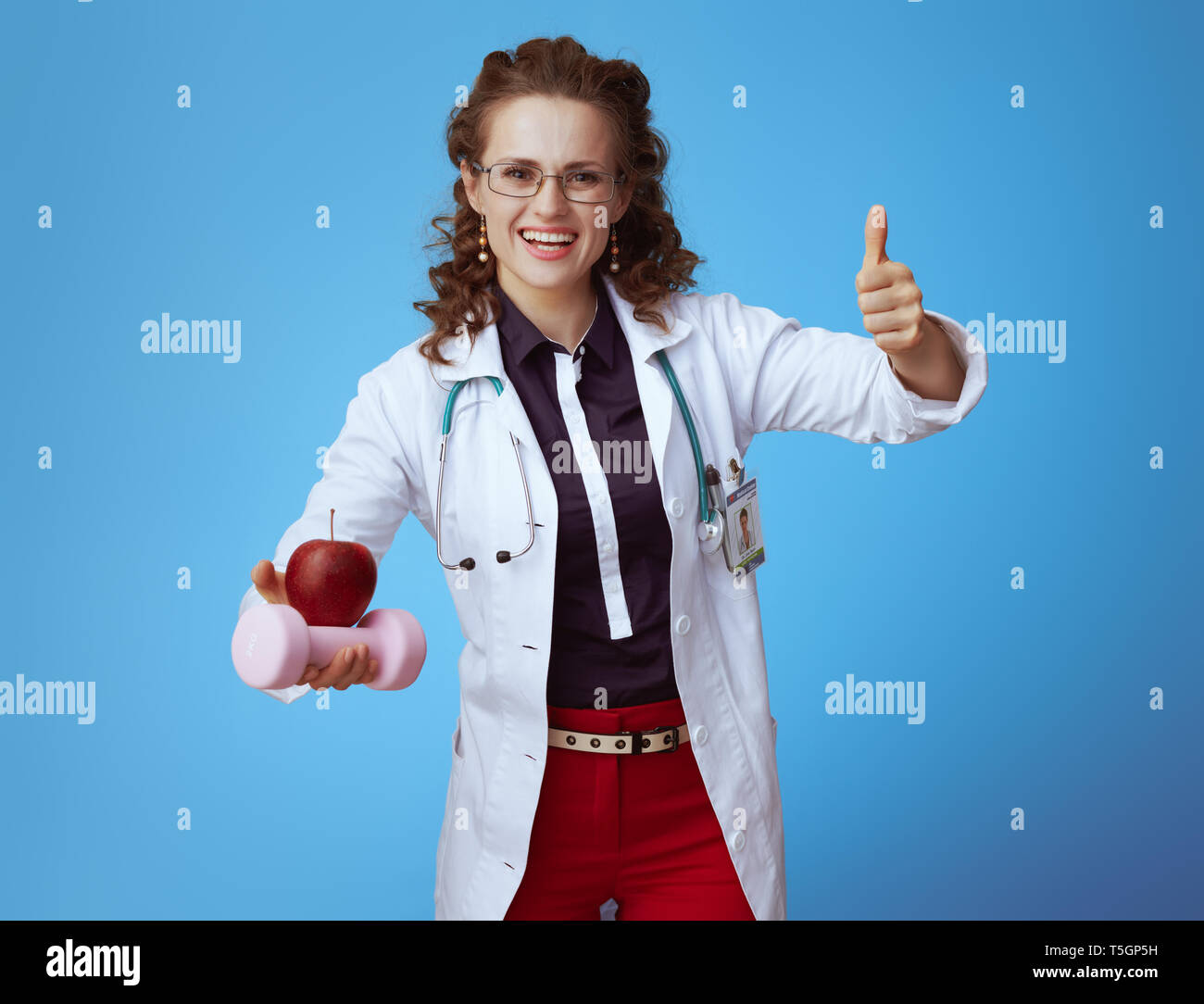 happy modern physician woman in bue shirt, red pants and white medical ...