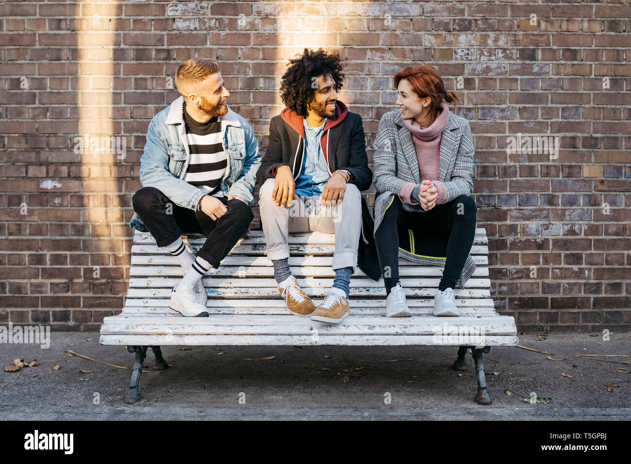 Three friends talking on a bench in front of a brick wall Stock Photo ...
