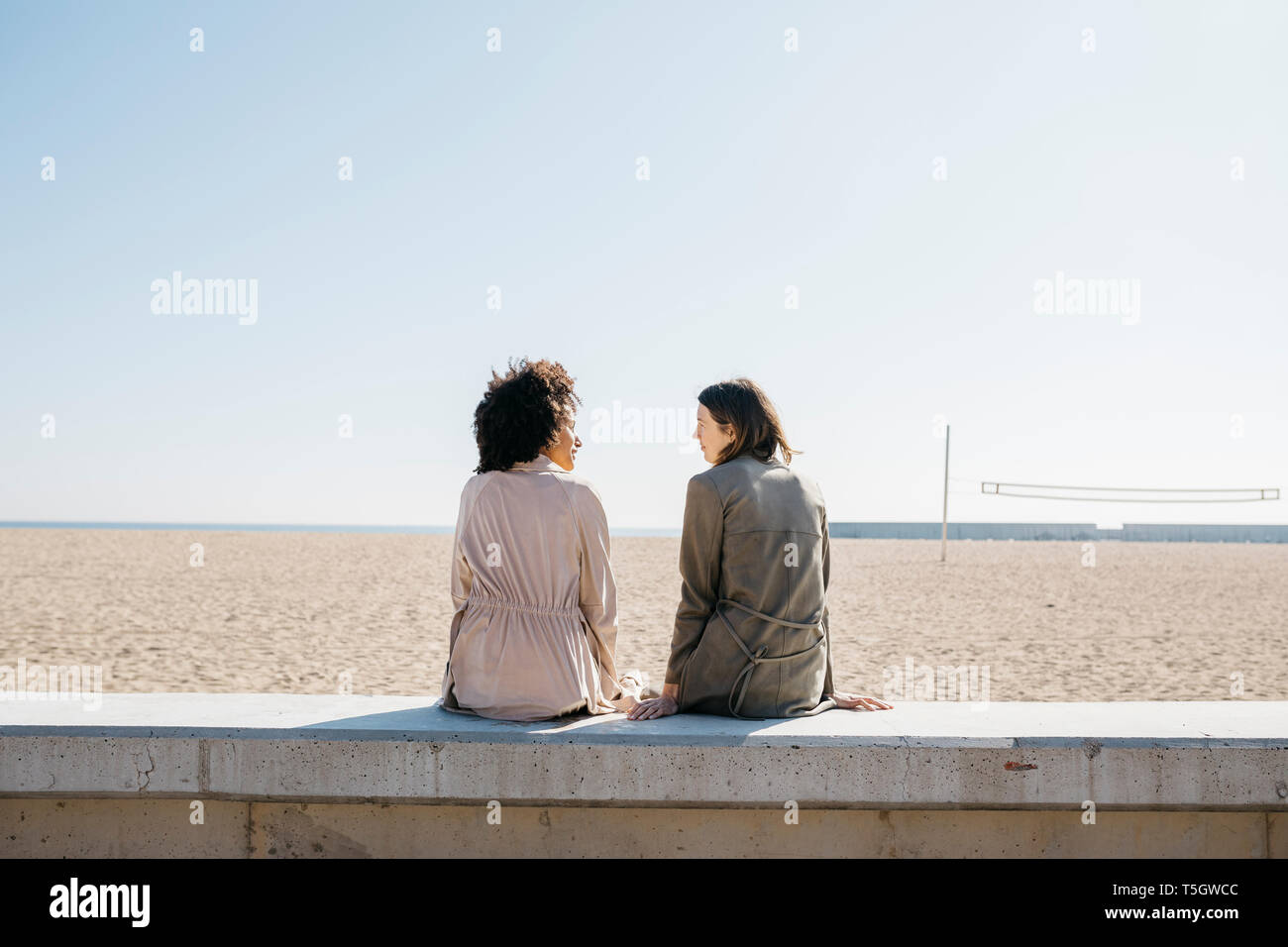 Back view of two friends sitting on the promenade enjoying leisure time ...