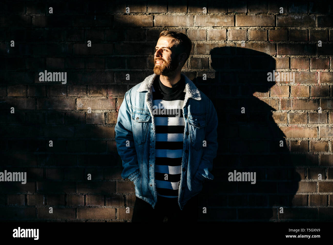 Smiling man standing at a brick wall in shadow Stock Photo - Alamy