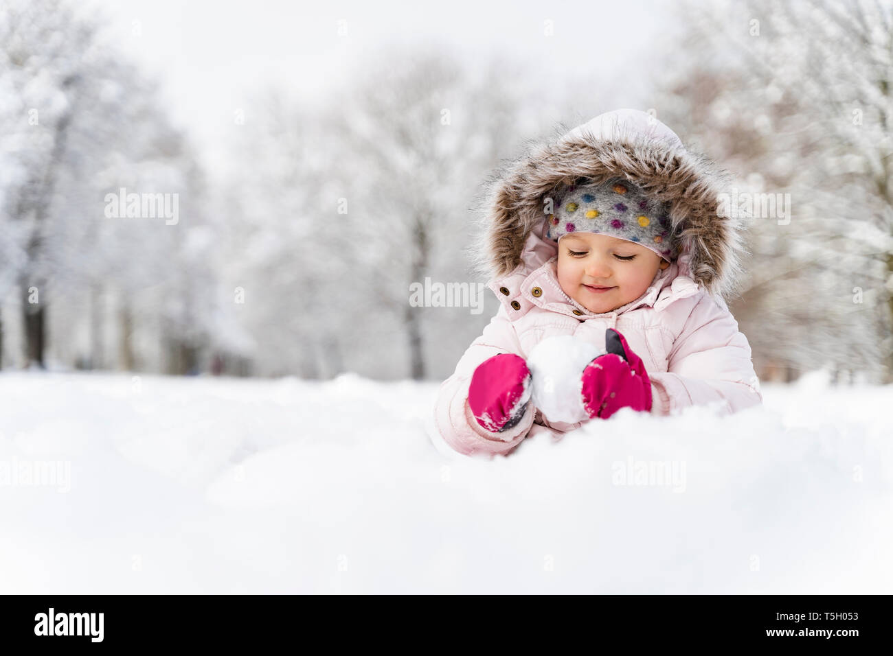 Cute little girl playing with snow in winter Stock Photo - Alamy