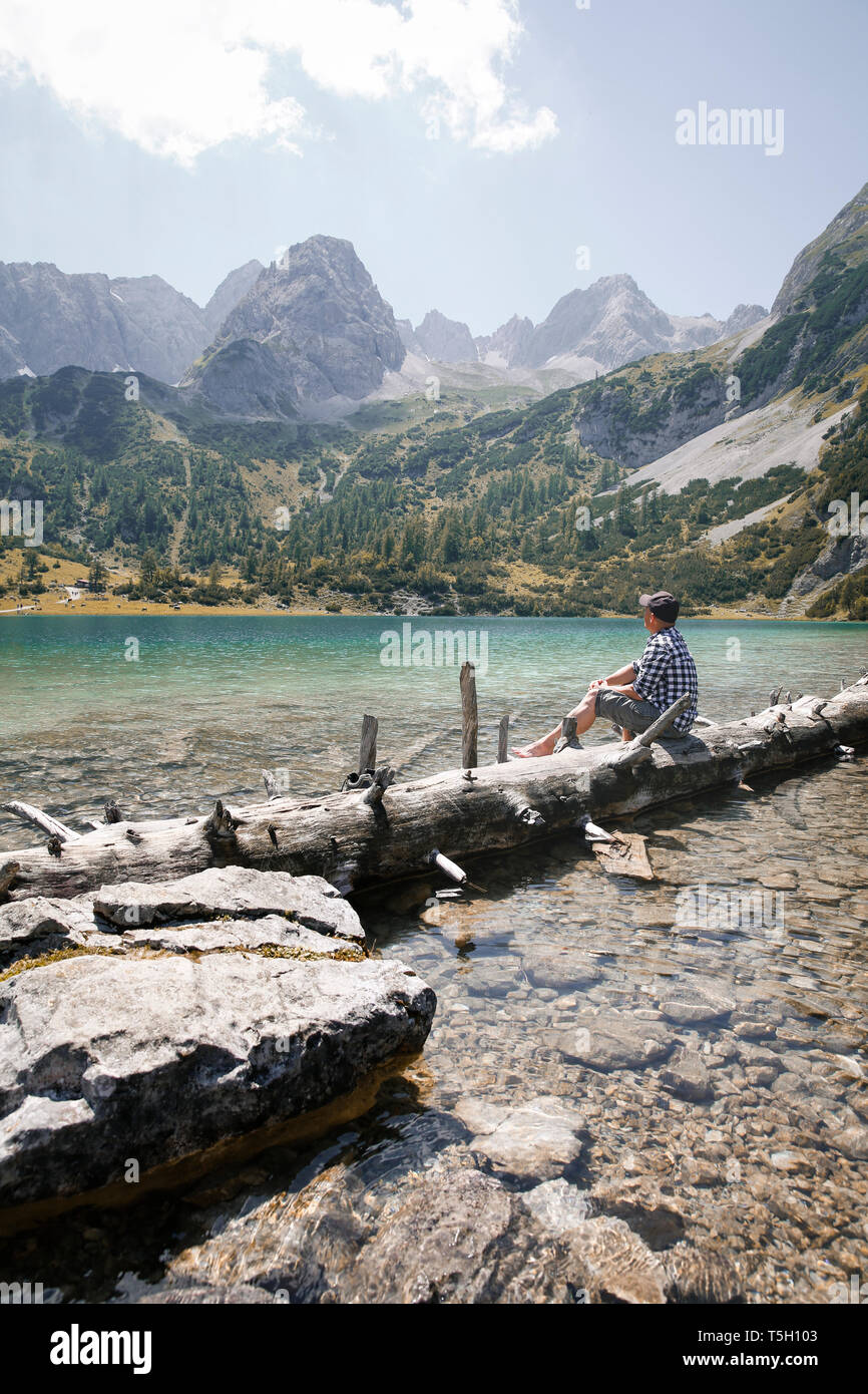 Austria, Tyrol, man sitting on tree trunk at lake Seebensee Stock Photo ...