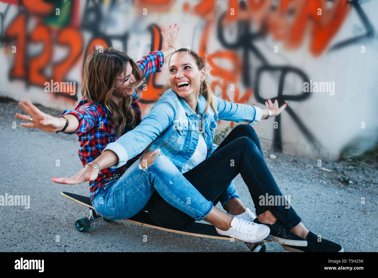 Two laughing friends sitting on longboard with arms outstretched Stock ...