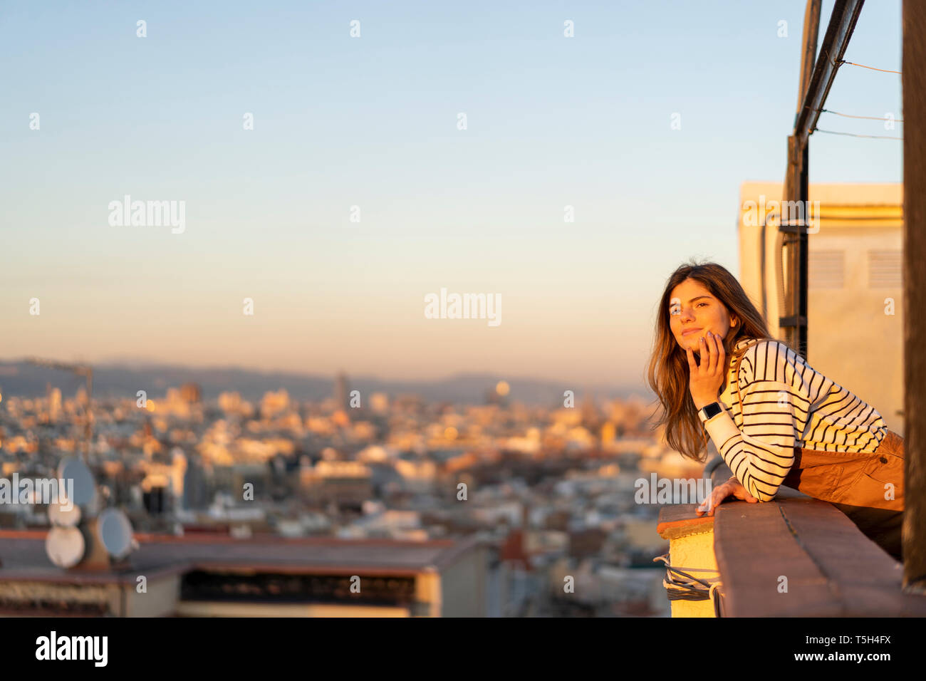 Portrait of content young woman relaxing on roof terrace at sunset ...