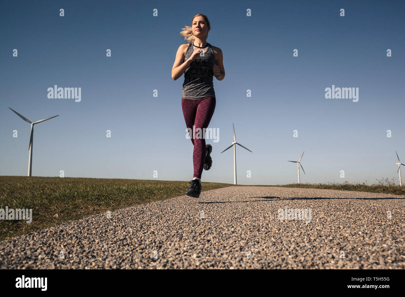 Young woman jogging on field way, wind wheels in the background Stock ...