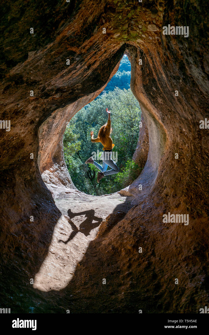 Young woman jumping in cave entrance, Cova Simanya,Barcelona, Spain ...