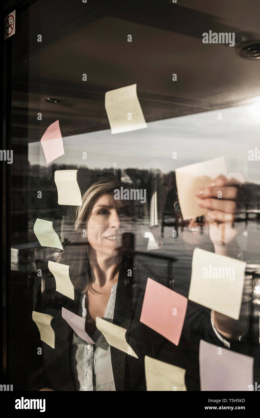 Two businesswomen brainstorming, putting sticky notes on window pane ...