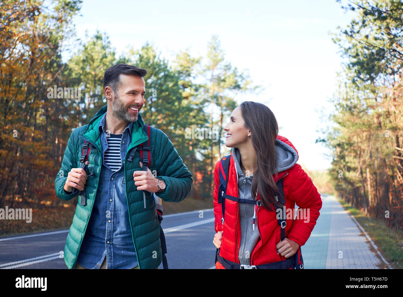 Happy couple walking along road in the woods during backpacking trip ...