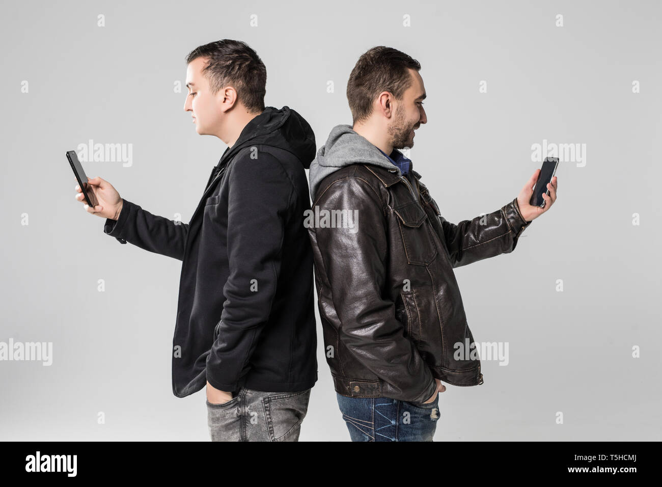 Two casual man standing sideby side with phones in hands isolated on ...