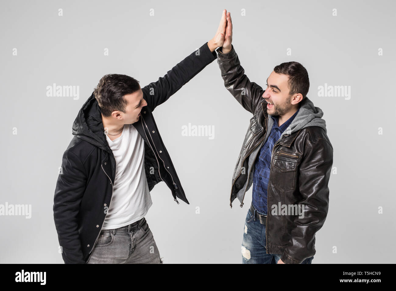 Portrait of two delighted young men celebrating with high five gesture ...