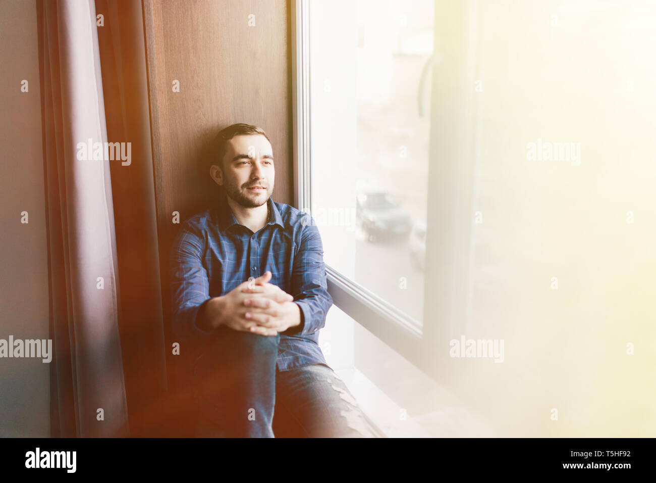 Handsome young man sitting on windowsill Stock Photo - Alamy